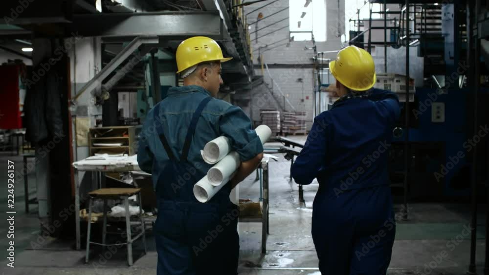 Rear view follow shot of male factory worker in overalls and hardhat ...