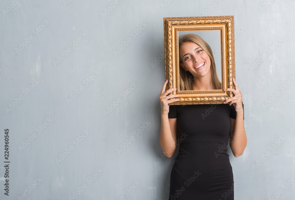 Beautiful young woman over grunge grey wall holding vintage frame with ...