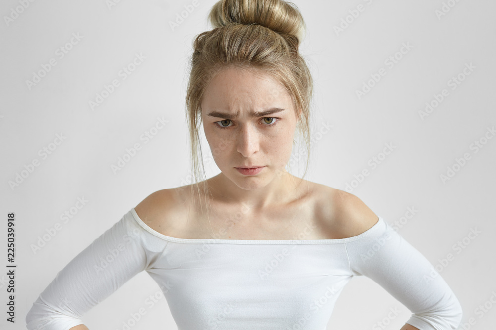 Studio shot of angry grumpy young European female with messy hairstyle ...