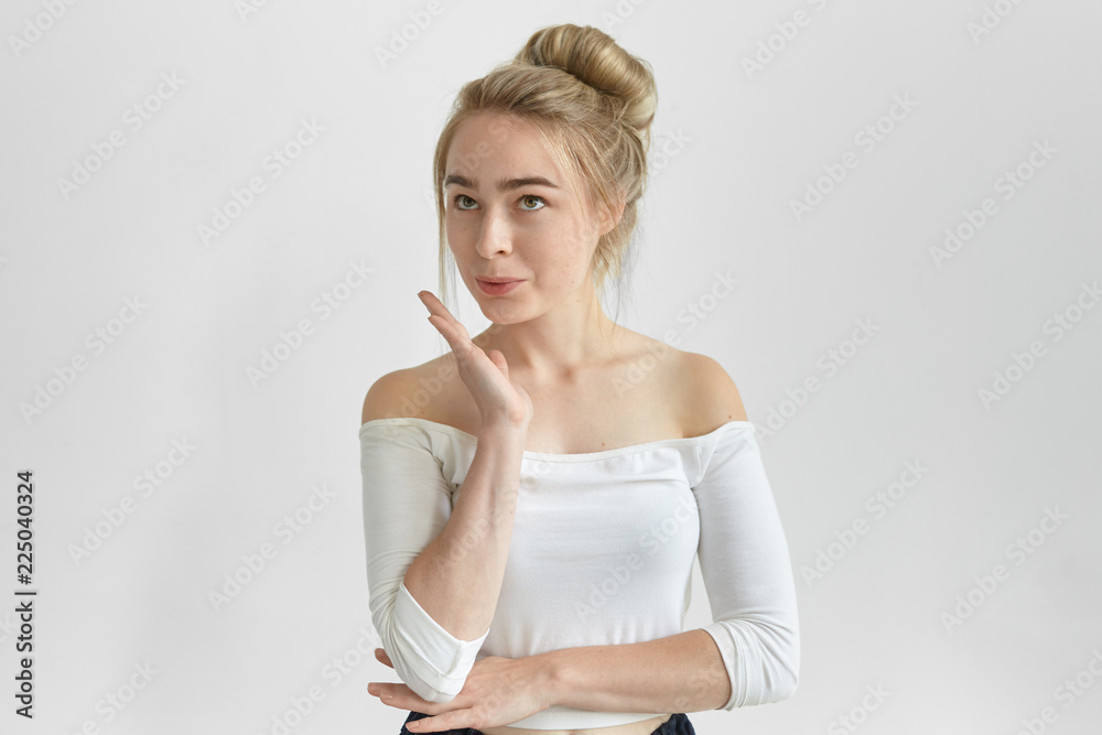 Studio shot of emotional stylish young female with hair knot holding ...