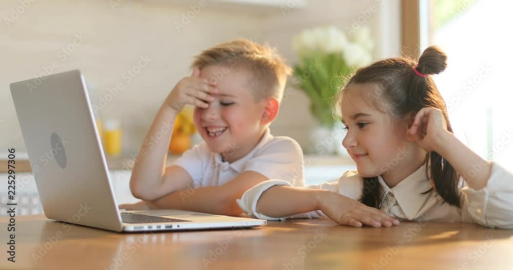 Portrait of two smiling school kids using laptop computer in kitchen ...