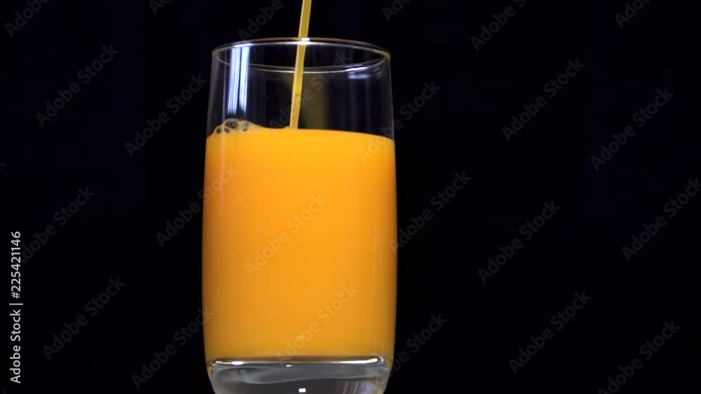 Pouring orange and yellow juice into a glass beaker. Behind the black ...