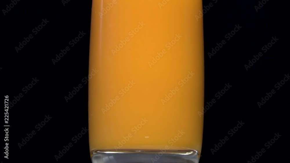 Pouring orange and yellow juice into a glass beaker. Behind the black ...