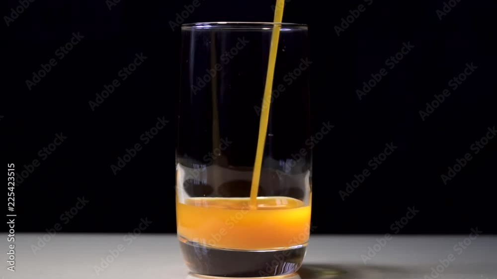 Pouring orange and yellow juice into a glass beaker. Behind the black ...