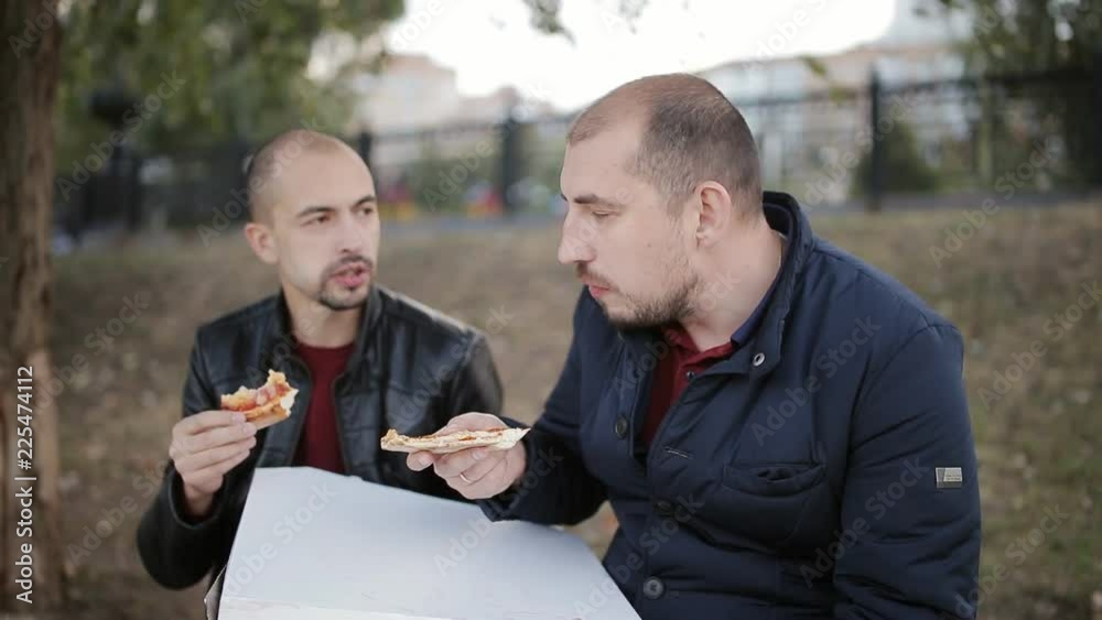 Two men on a Park bench eating a takeaway pizza from the box Stock ...