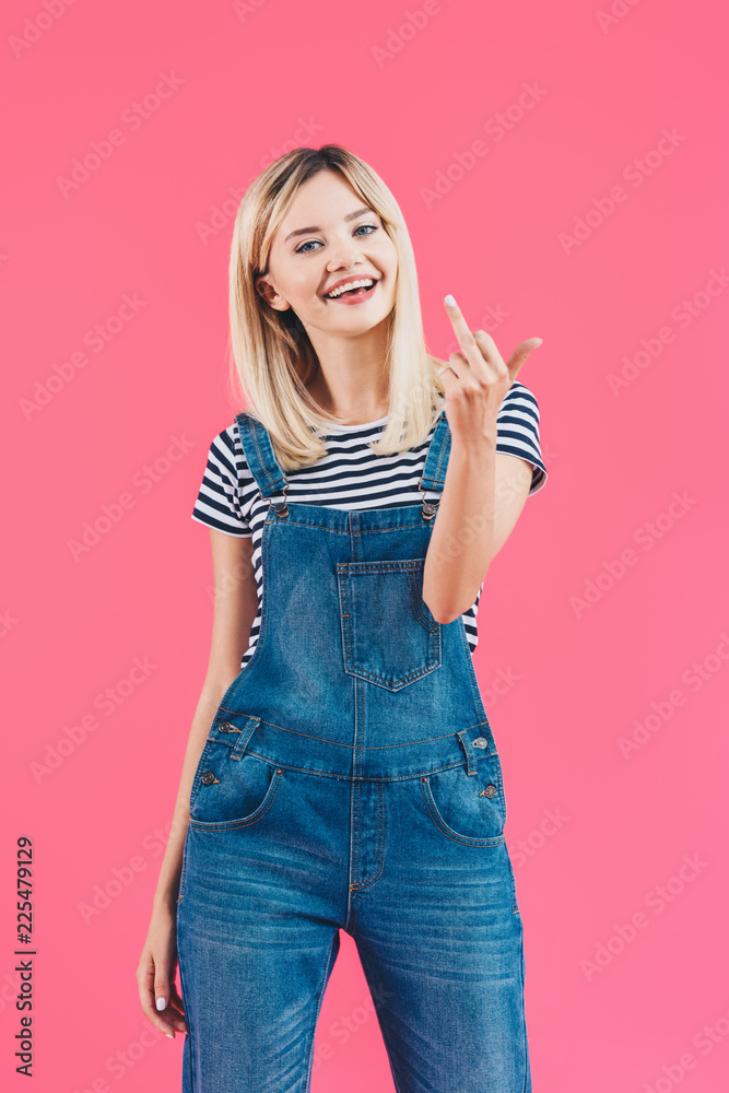 smiling beautiful girl in denim overall showing middle finger isolated ...