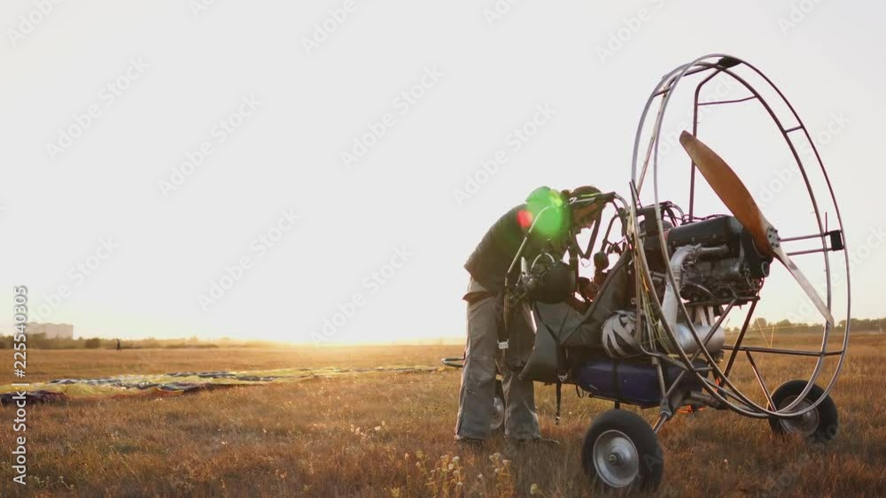 The motor paraglider stands in the field at sunset with a wooden ...