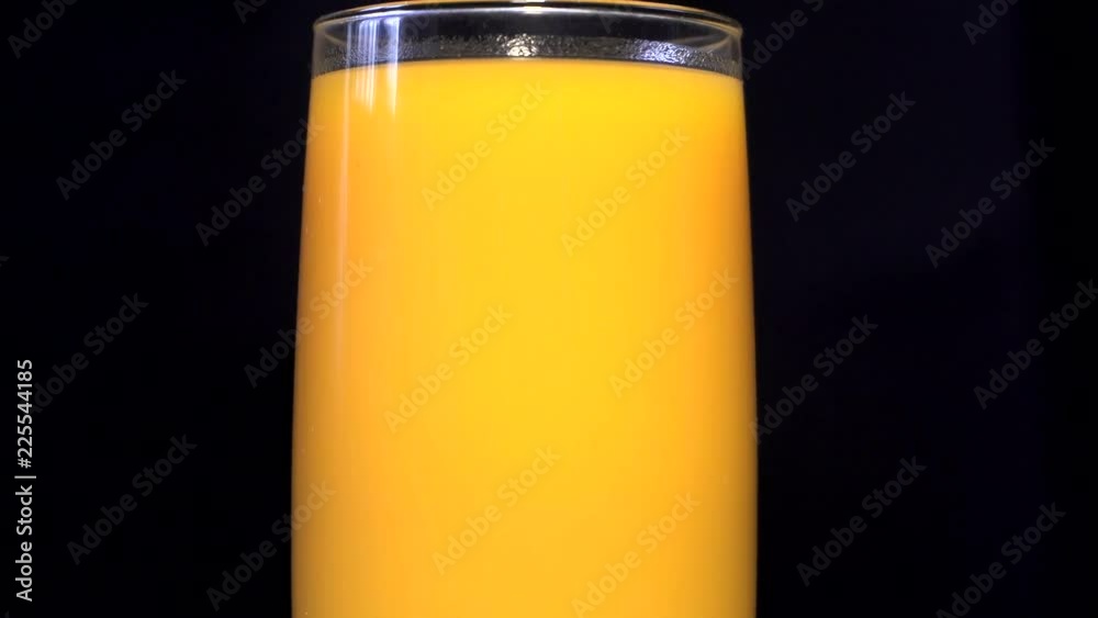 Pouring orange and yellow juice into a glass beaker. Behind the black ...