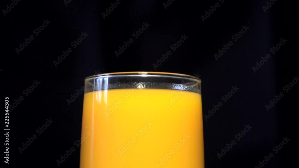 Pouring orange and yellow juice into a glass beaker. Behind the black ...