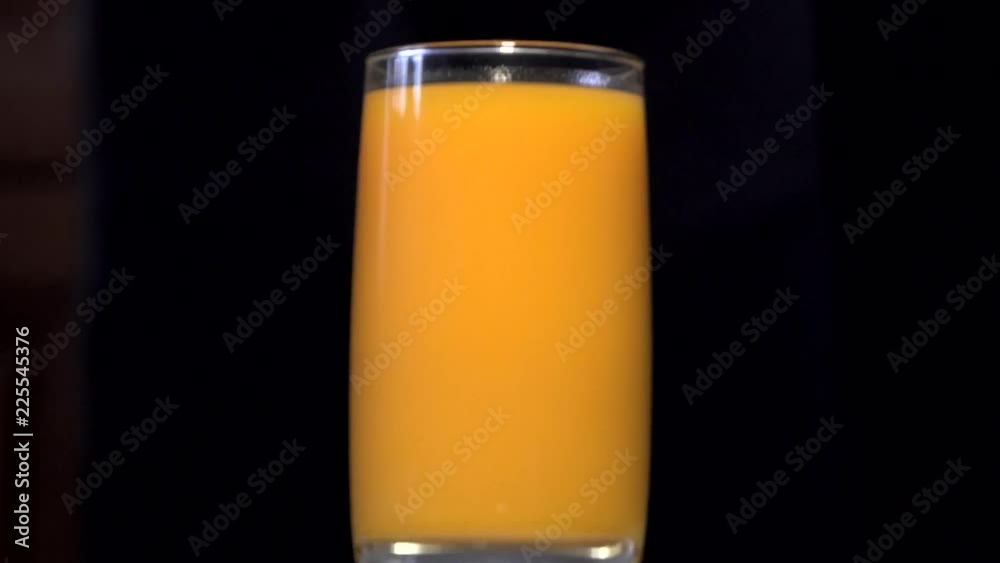 Pouring orange and yellow juice into a glass beaker. Behind the black ...
