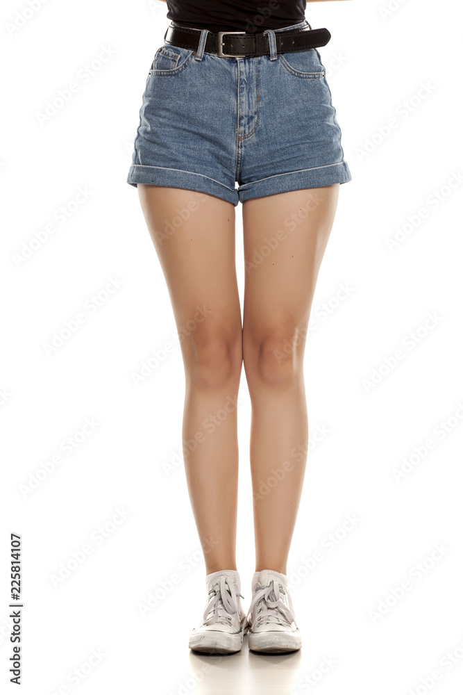 Female legs in short jeans and sneakers standing on white background ...