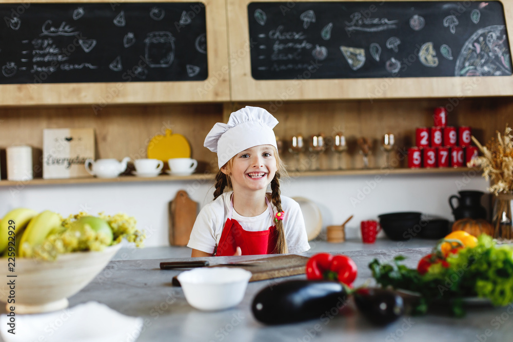 Little chief on a kitchen. Charming little girl in a chief hat stands ...