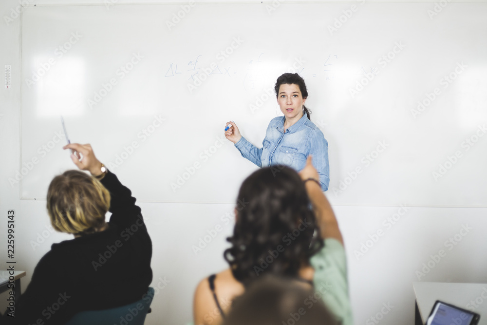 Students pointing at teacher standing against whiteboard in classroom ...
