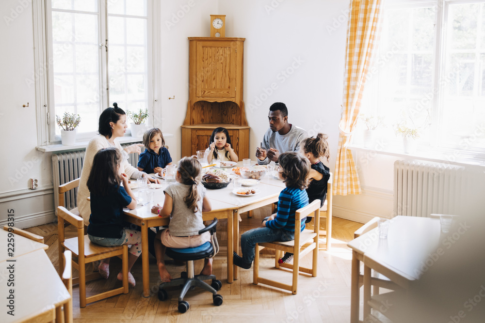 Teachers and students eating lunch at table in kindergarten Stock Photo ...