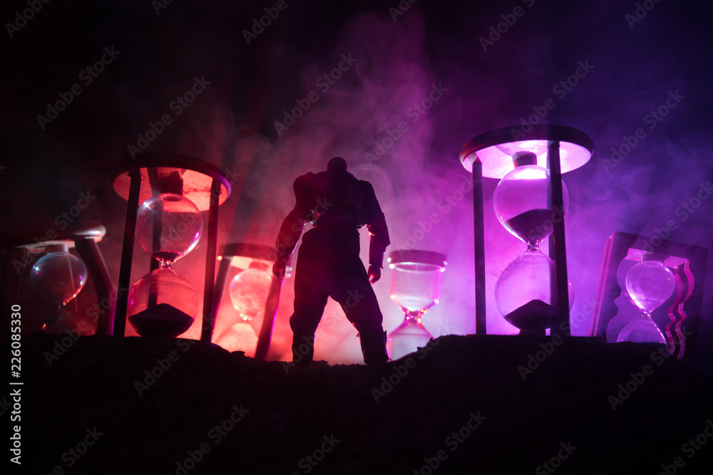 Time Concept Silhouette Of A Man Standing Between Hourglasses With Smoke And Lights On A Dark