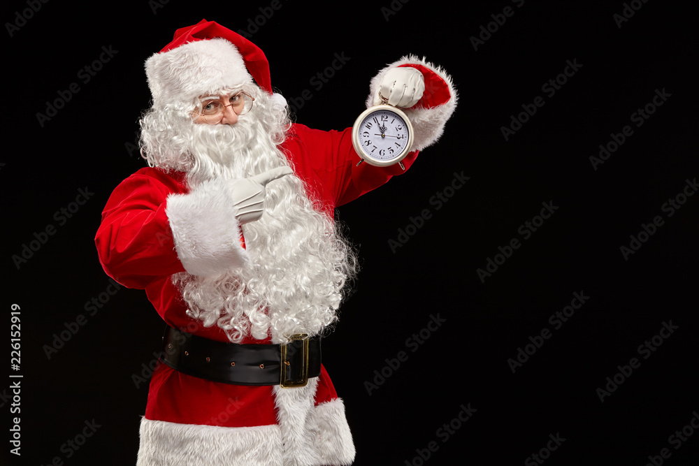 Santa Claus on a black background points his finger at the clock ...