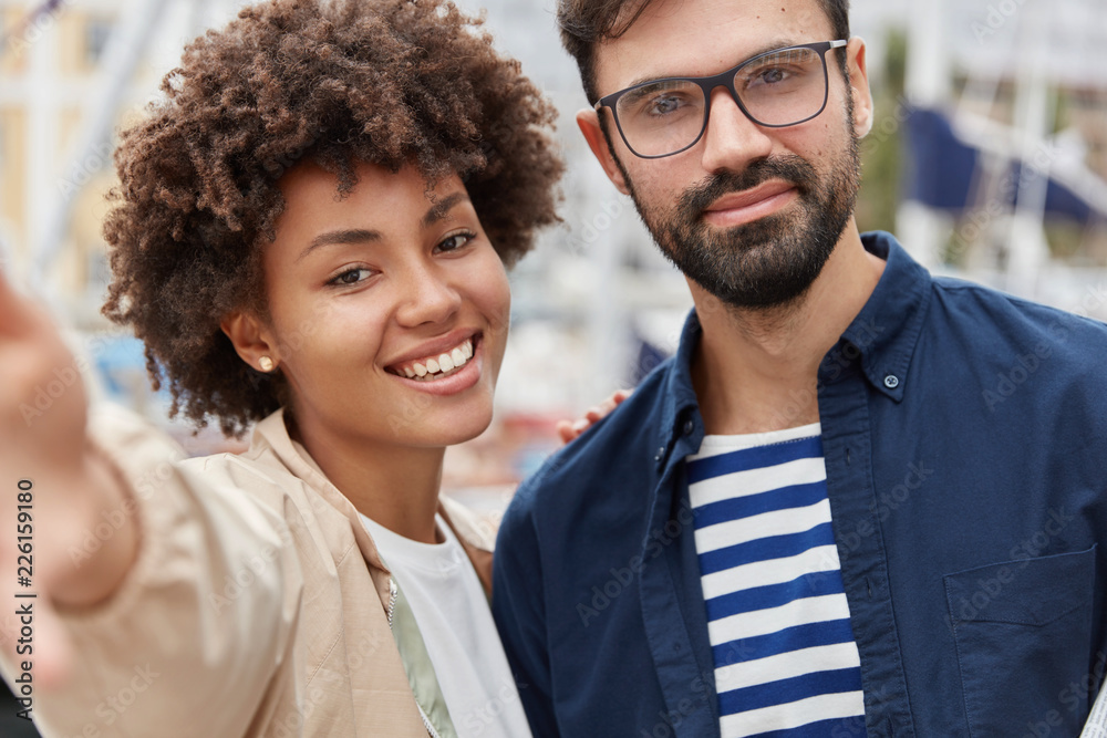 Outdoor shot of lovely mixed race couple have stroll together, stand ...