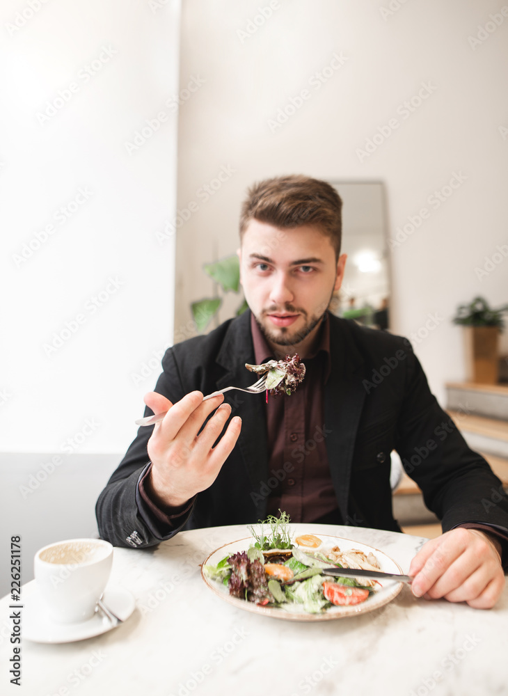 Handsome man sits from a cozy light restaurant and eats a plate salad ...