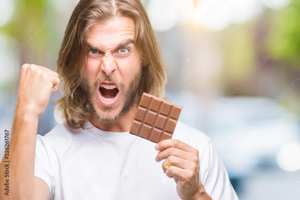 Young handsome man with long hair eating chocolate bar over isolated ...