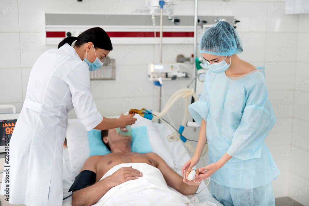 Medical team. Unconscious middle aged man lying in hospital bed and ...