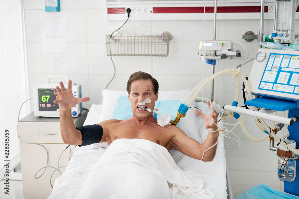 Portrait of enraged patient on mechanical ventilator lying in bed and ...