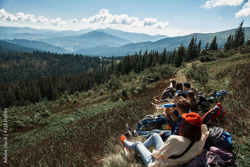 Group of active travelers sitting on the mountain hills while rejoicing ...