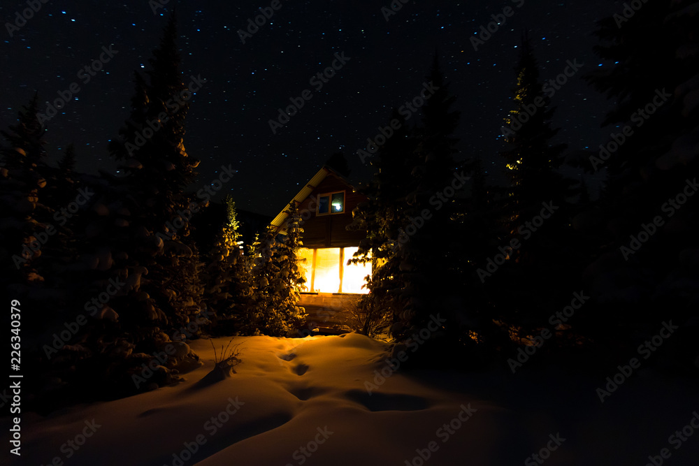 Light from the window of a forest hut under the night sky of the milky ...