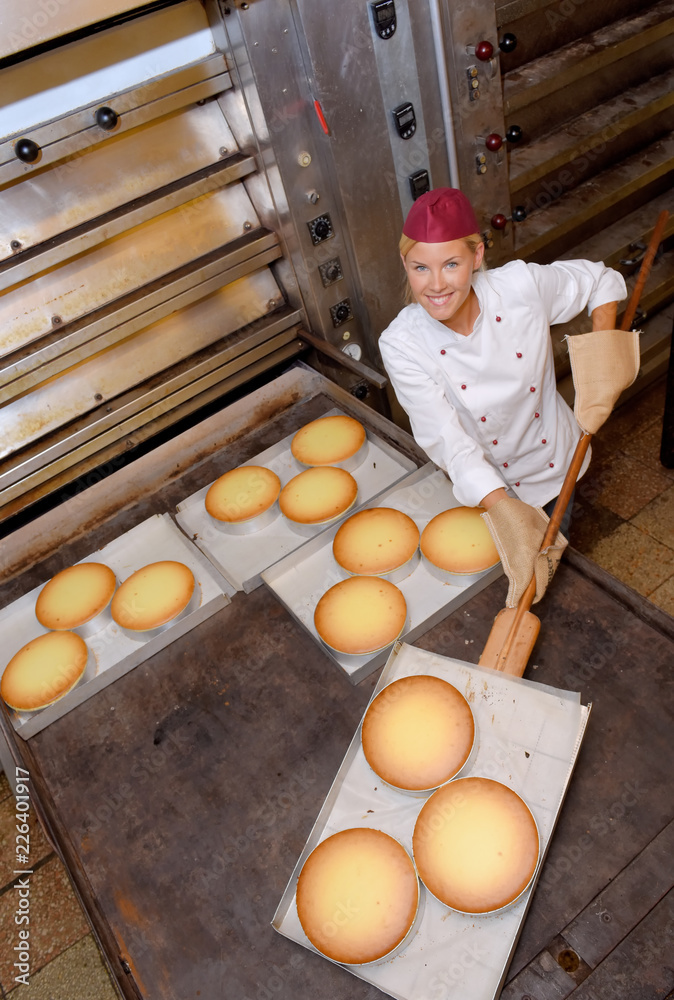 A young baker girl takes up her work in a bakery. She poses for the ...
