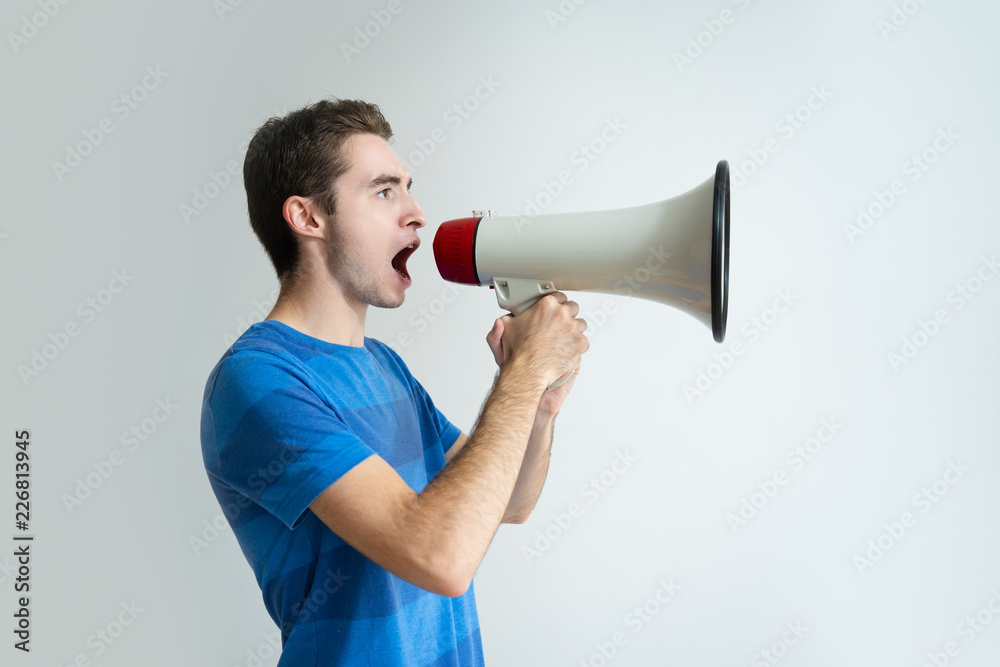 Serious man holding megaphone and screaming into it. Young guy looking ...