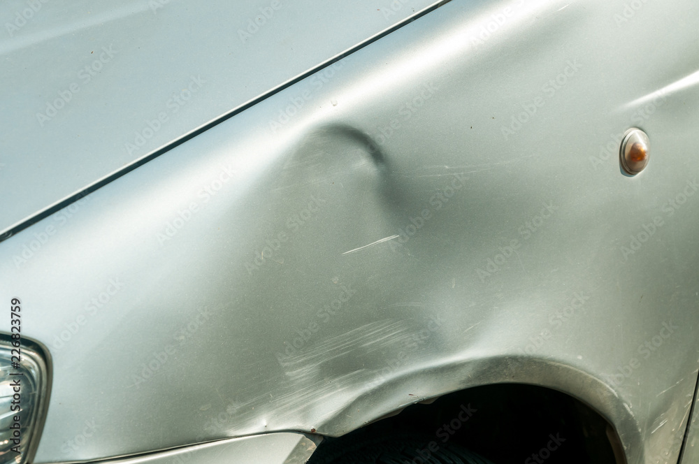 Dented sheet metal on the side of the silver car damaged in crash ...