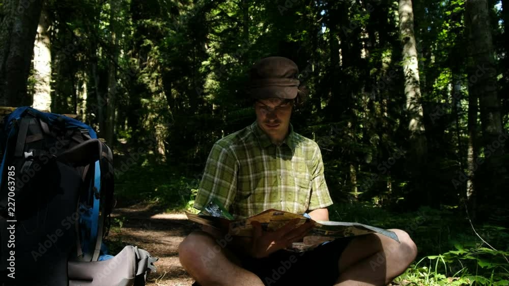 Young man tourist with a backpack sits in the forest checks the route ...