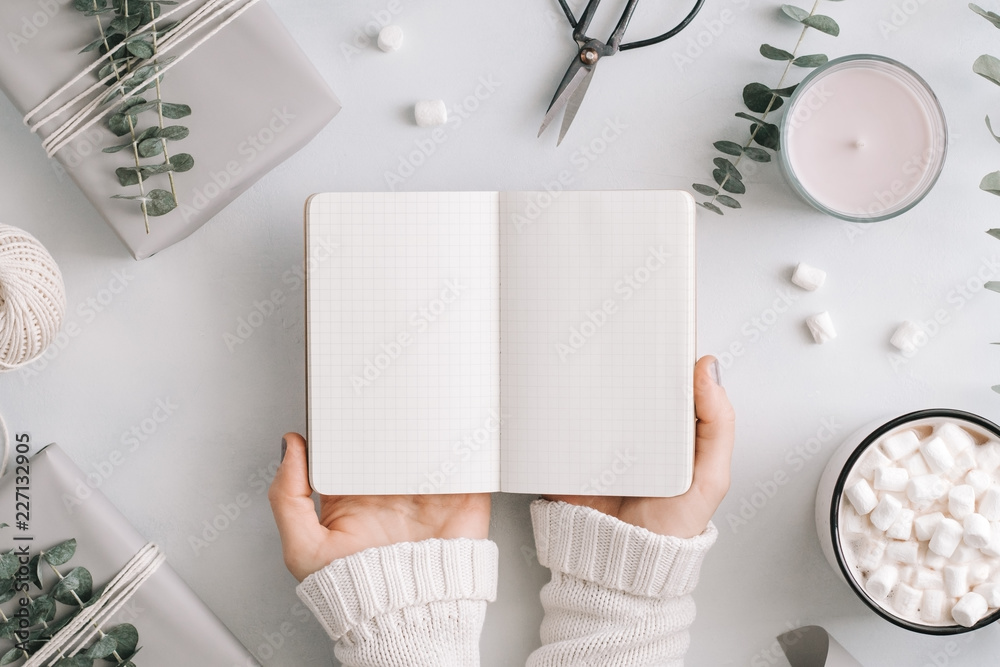 Girl's hands hold an blank notebook among gift boxes and winter festive ...