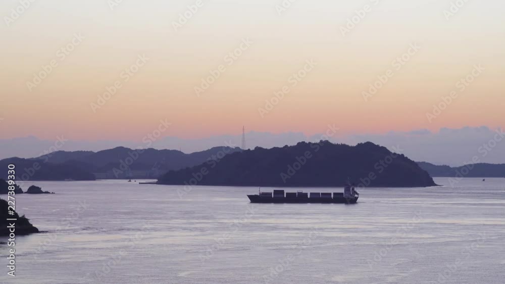 A cargo ship floats in a bay in Japan near Hiroshima at sunset. Near ...