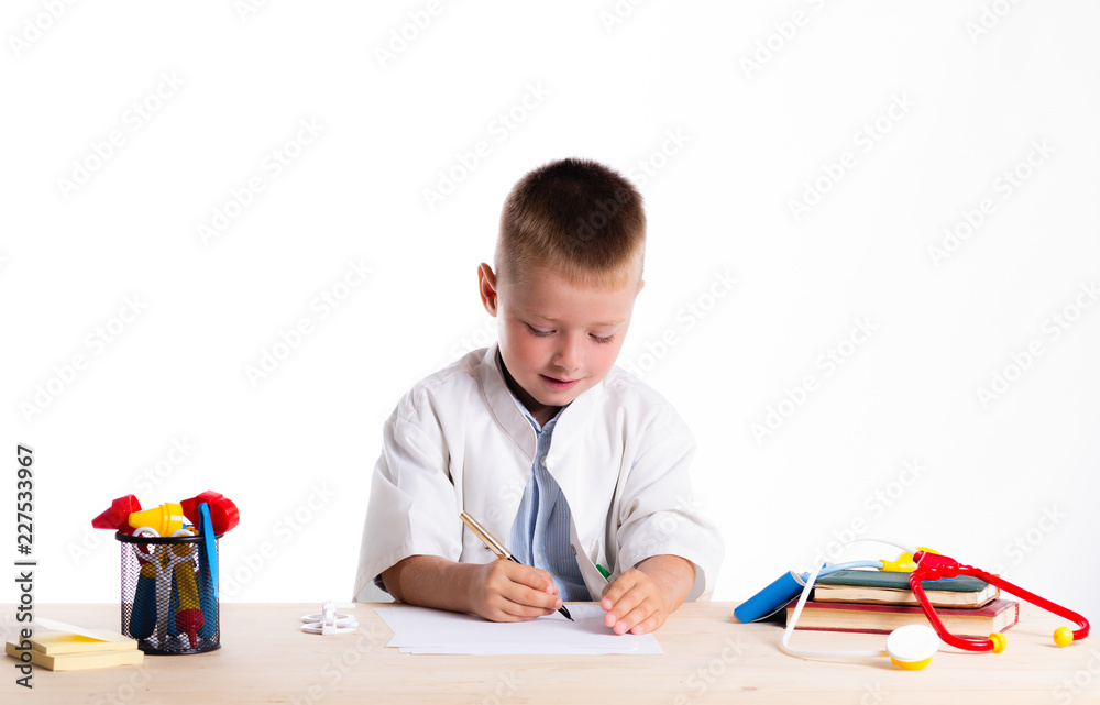 Cute little doctor boy with smile on face sitting at his desk on white ...