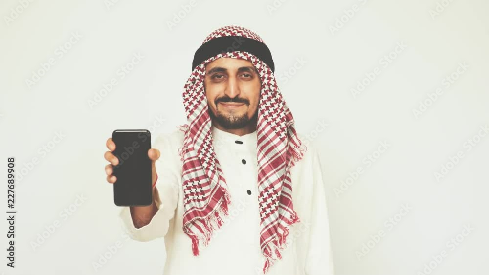 Smiling Arab in national dress shows smartphone and smiles. The man ...