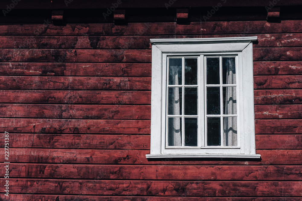 A white window on the wooden cottage of dark red and brown planks ...