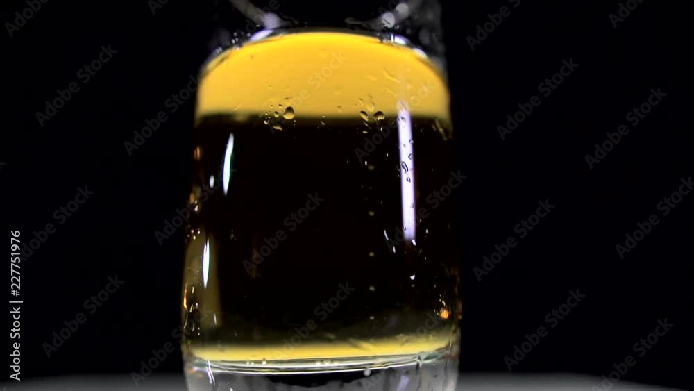 Pouring light beer into a glass beaker in slow motion. Air bubbles rise ...