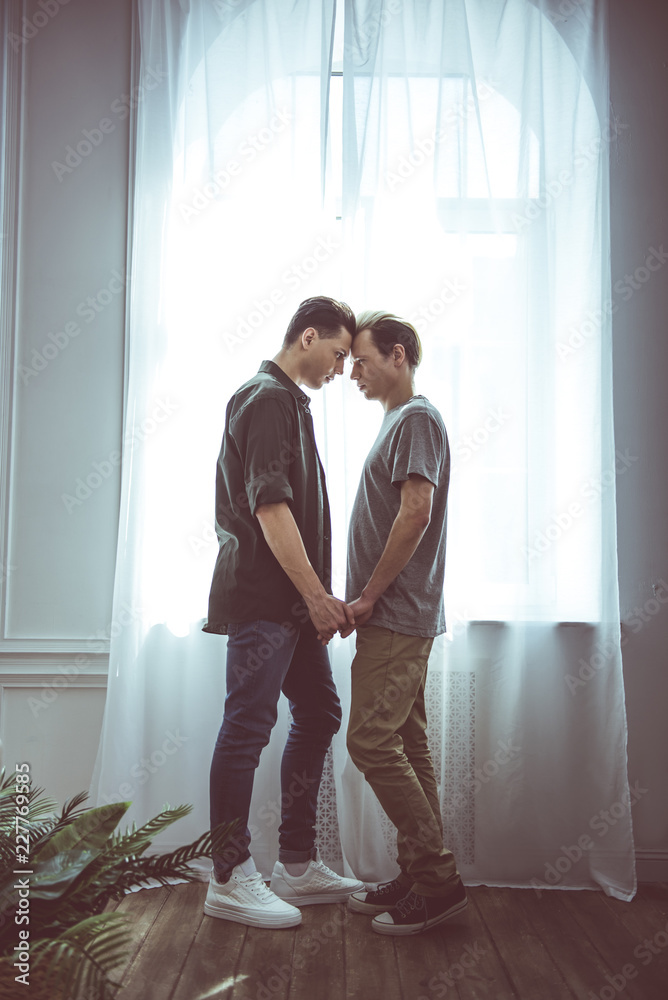 Full length side view portrait of two handsome guys holding hands and ...