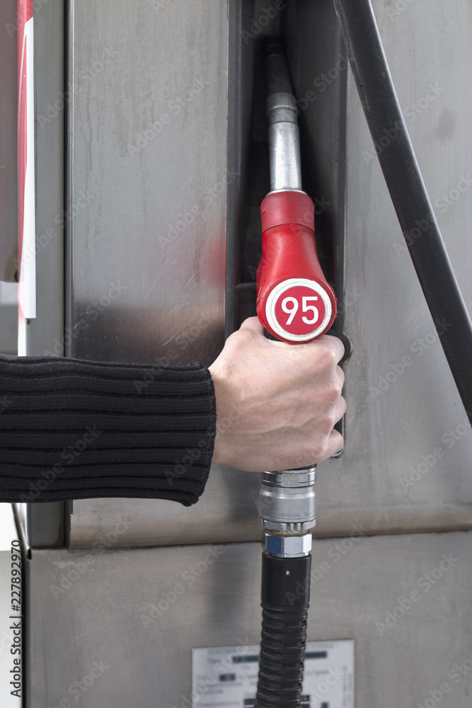 Male hand takes the fuel nozzle for refueling at a gas station ...