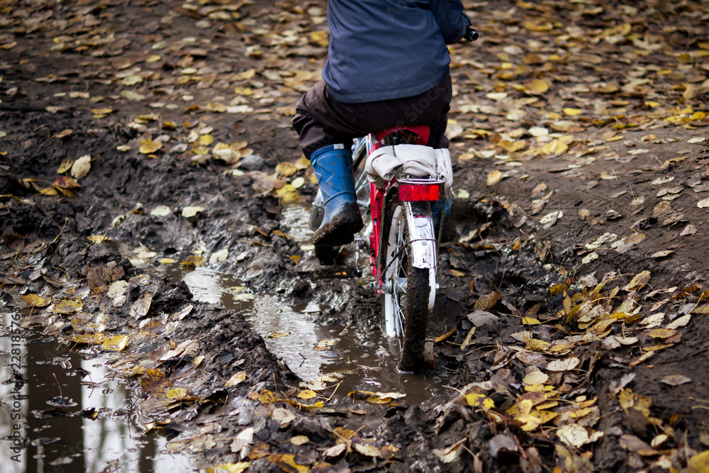 child rides a bike through a mud puddle in the mud in a forest in ...