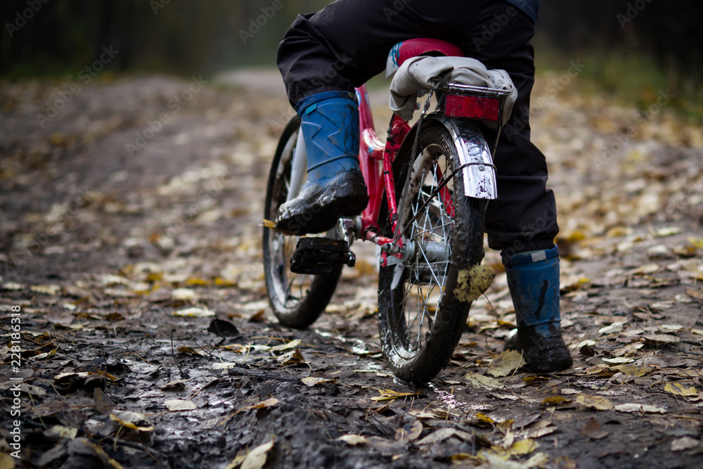 child rides a bike through a mud puddle in the mud in a forest in ...