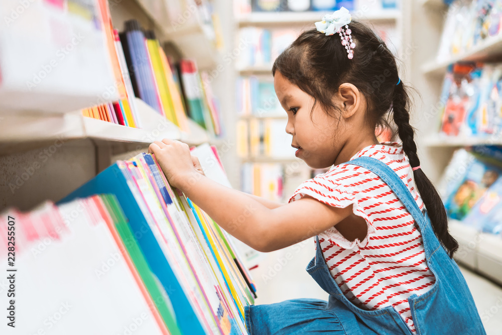 Cute asian child girl select book on bookshelf in bookstore in ...