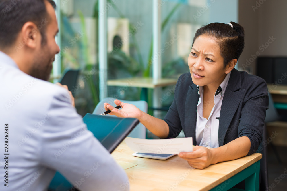 Displeased Asian female boss looking at Latin subordinate in confusion ...
