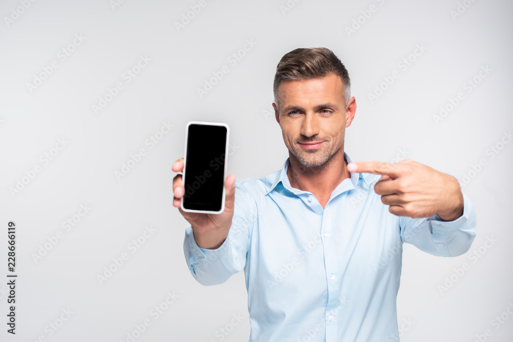 handsome adult man pointing at blank screen of smartphone isolated on ...
