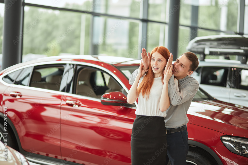 Caucasian charming couple stand in front of new red car in dealership ...