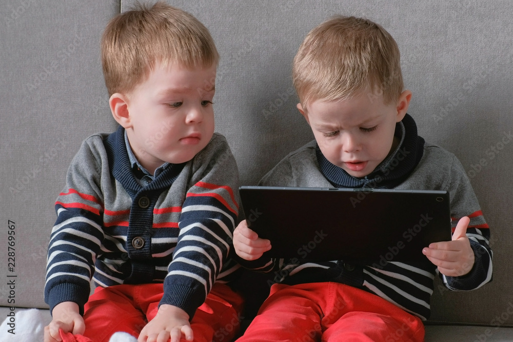 Two twin brothers take away each other's tablet sitting on the sofa ...
