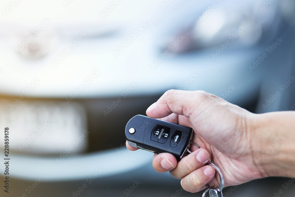 Man hand presses a button on the car remote control against blur car ...
