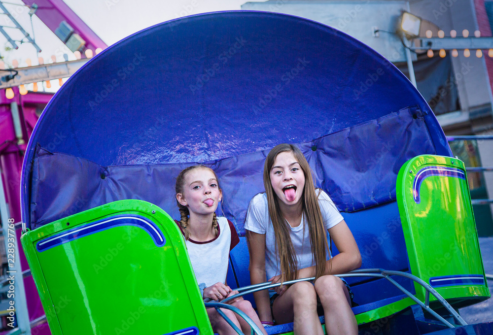 Two cute teen girls playing and having fun while riding an amusement ...