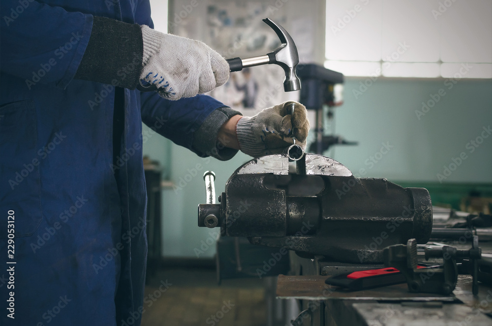 Man worker is working with iron detail by hammer on vise grip on ...