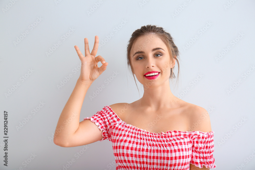 Beautiful young woman showing OK gesture on light background Stock ...